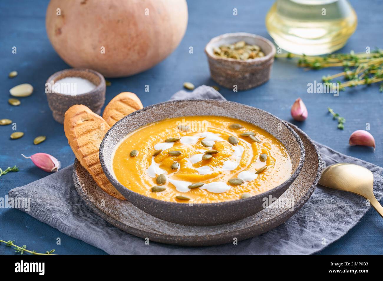 Pupmkin cream soup puree on dark bright blue wooden table, seeds, toast ...