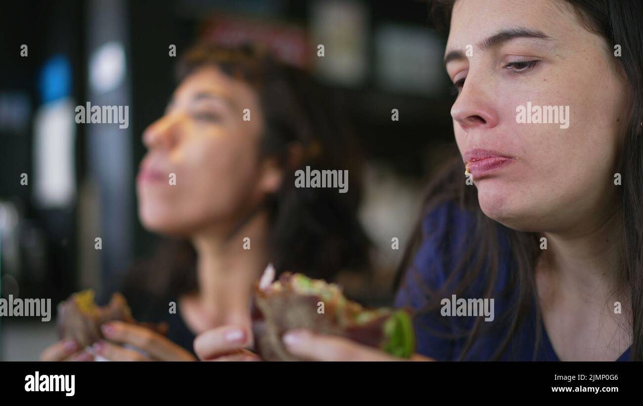 Two people eating burgers. Young women taking a bite of cheeseburgers ...