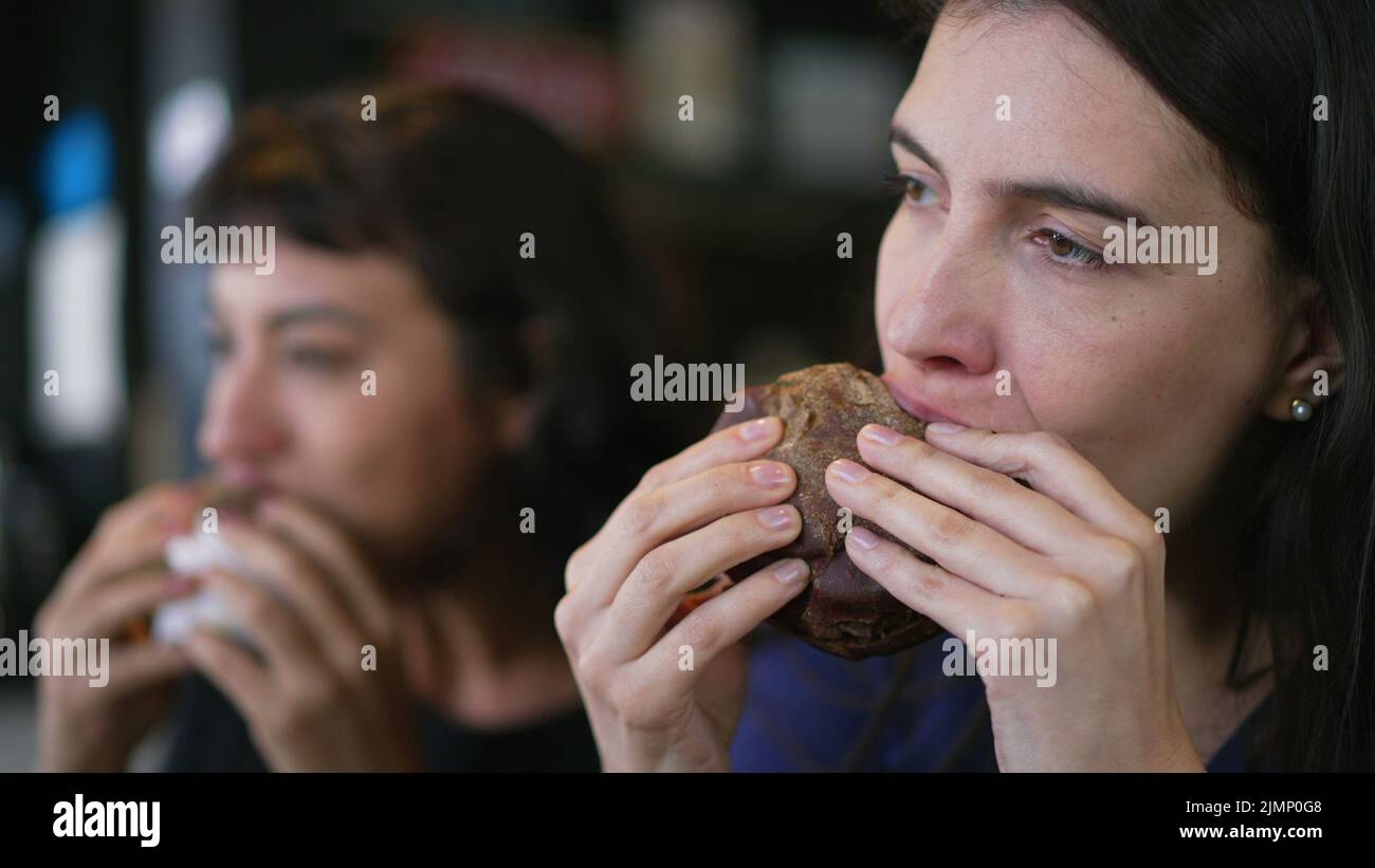 Two people eating burgers. Young women taking a bite of cheeseburgers ...