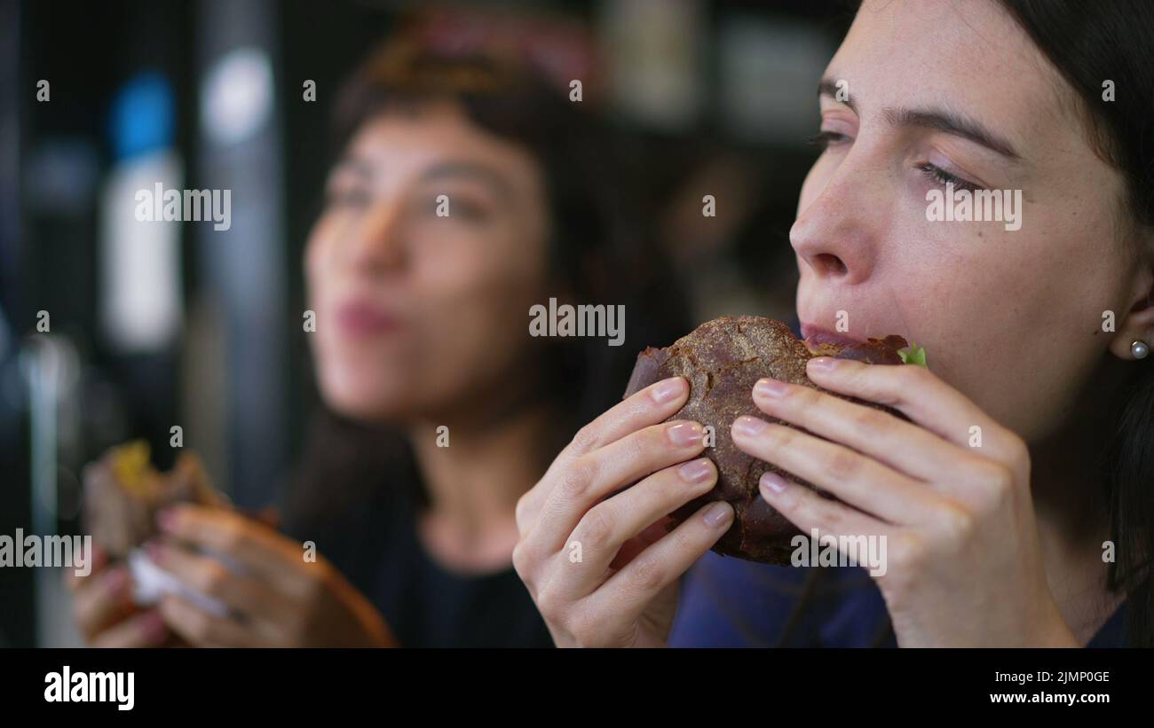 Two people eating burgers. Young women taking a bite of cheeseburgers ...