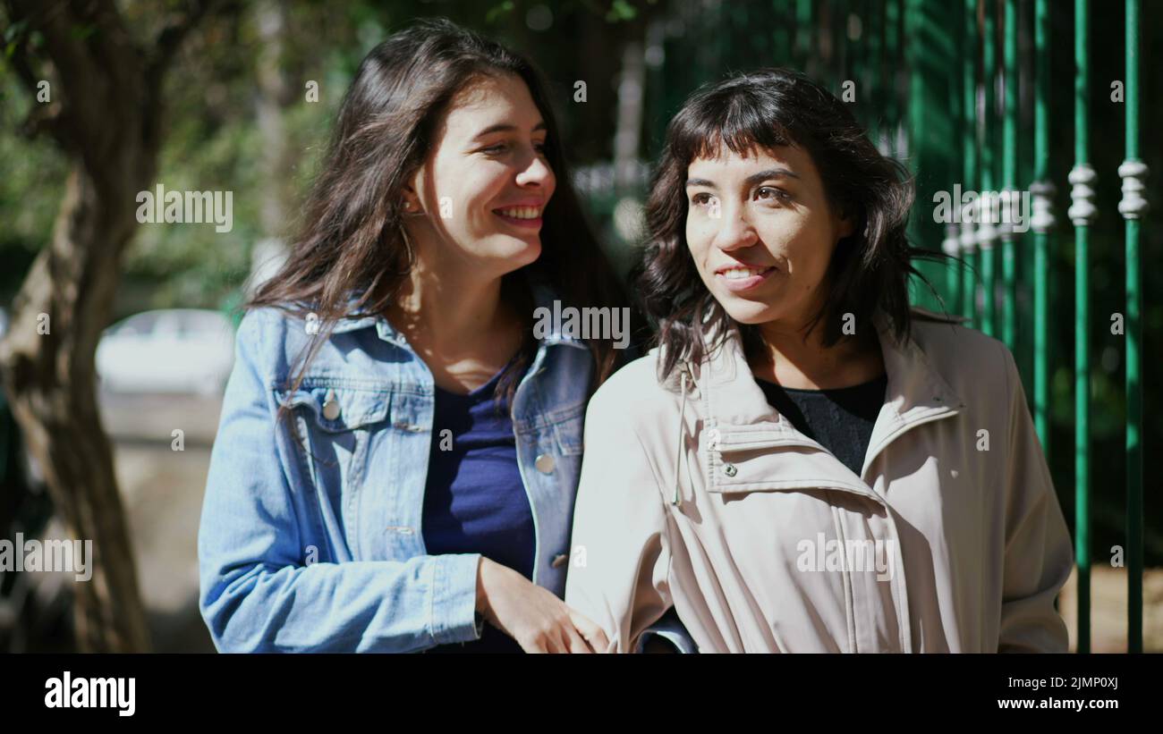 Two female friends gossiping walking together pointing with hand ...