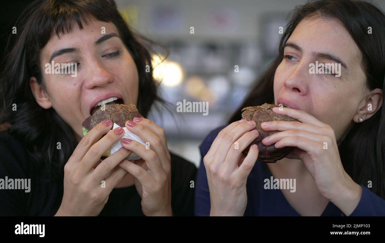 Two happy female friends eating burgers at the same time. Young women ...