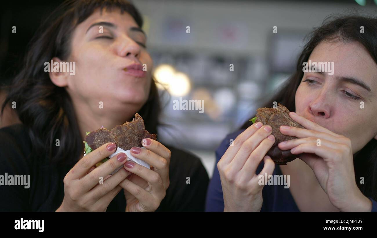 Two happy female friends eating burgers at the same time. Young women ...