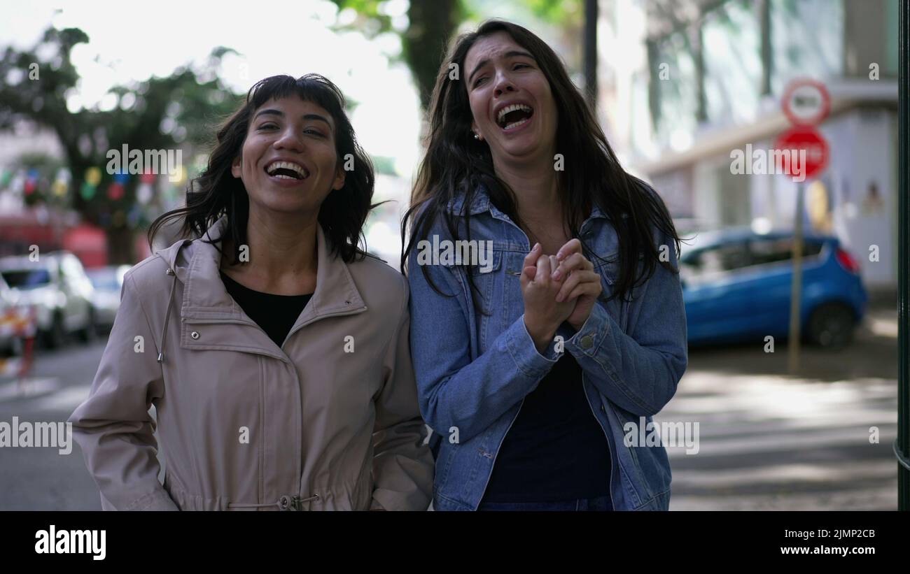Female friends laughing and smiling while while walking in city ...