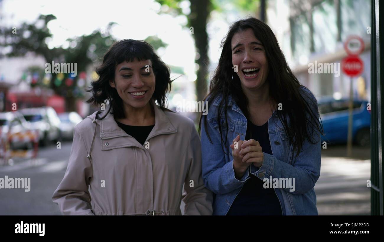 Female friends laughing and smiling while while walking in city ...