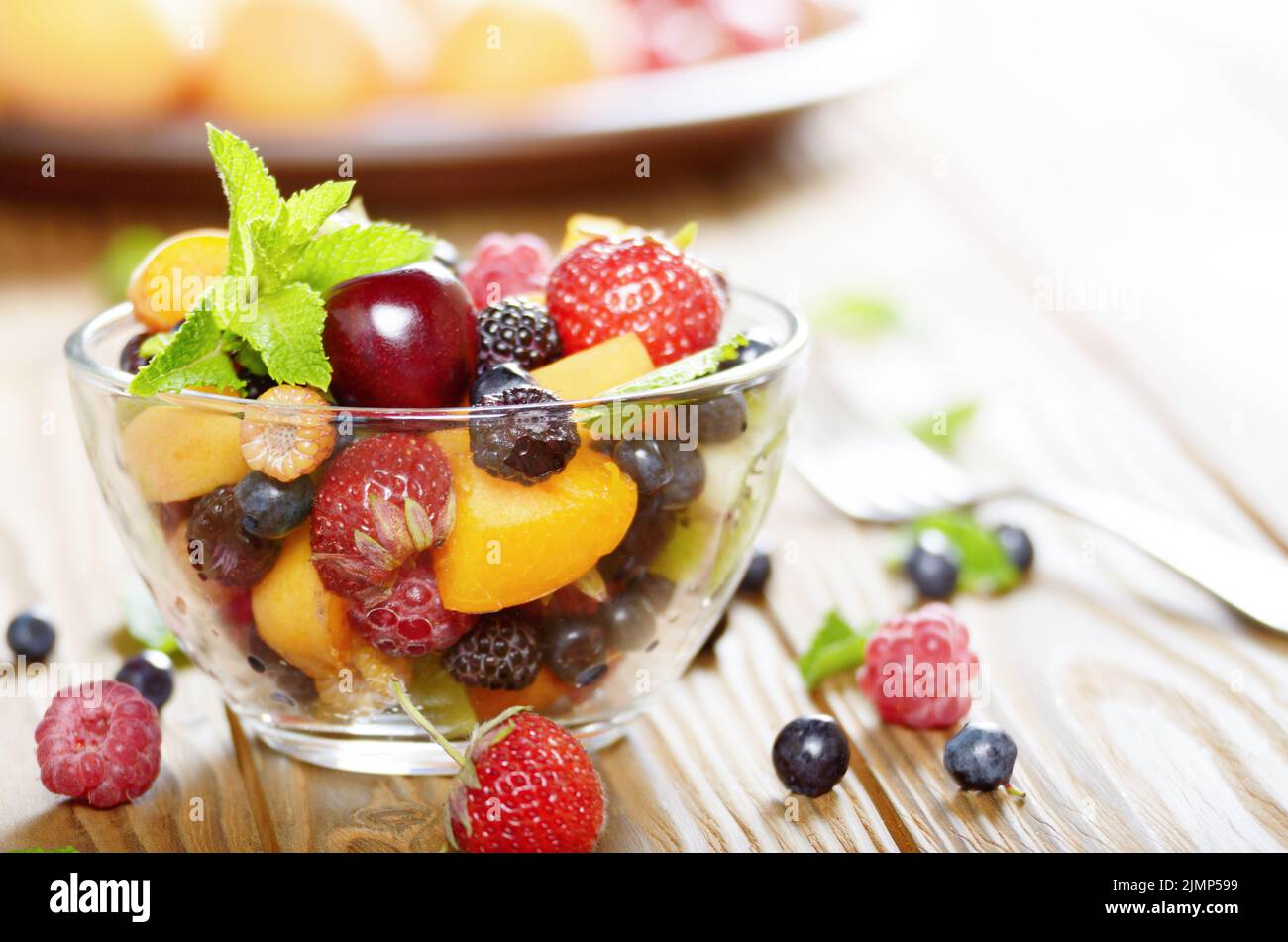 Assorted fruits in glass bowl on kitchen wooden table with fork aside ...