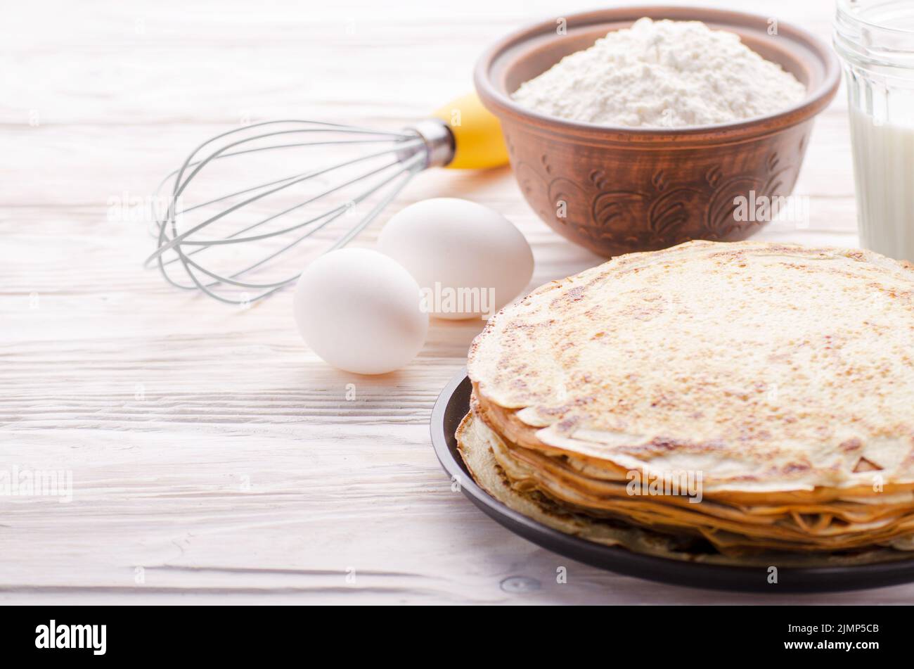 Stack of French crepes in frying pan on wooden kitchen table with milk ...