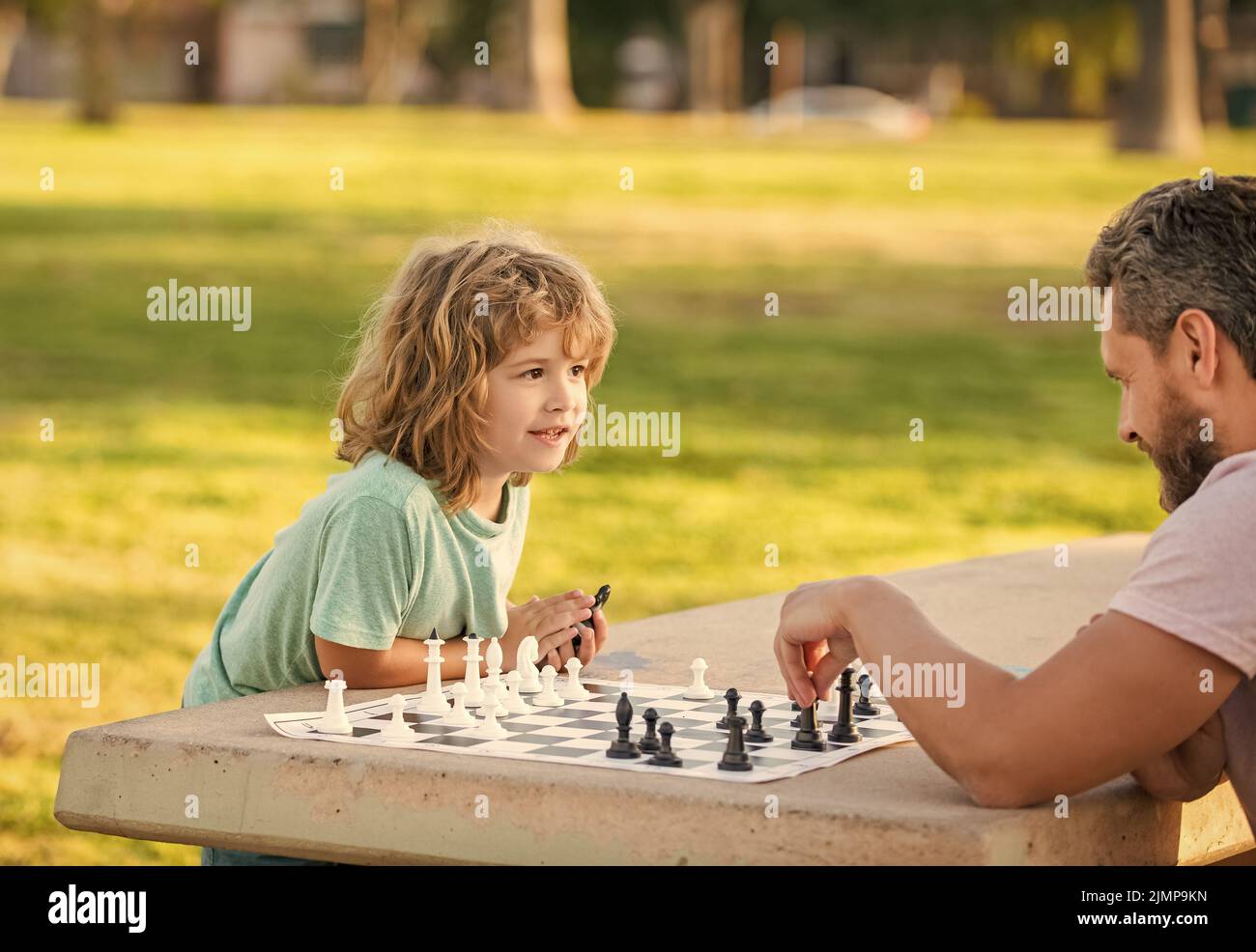 happy family of dad and son boy playing chess on table in park outdoor ...