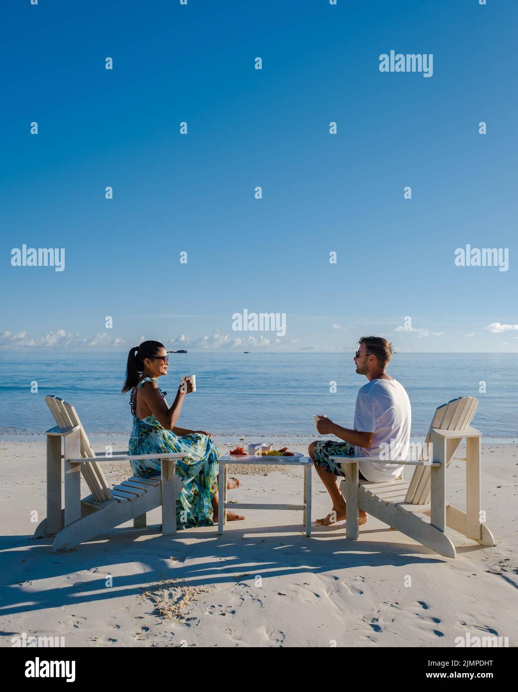 Couple men and women on the beach having coffee and fruit for breakfast ...