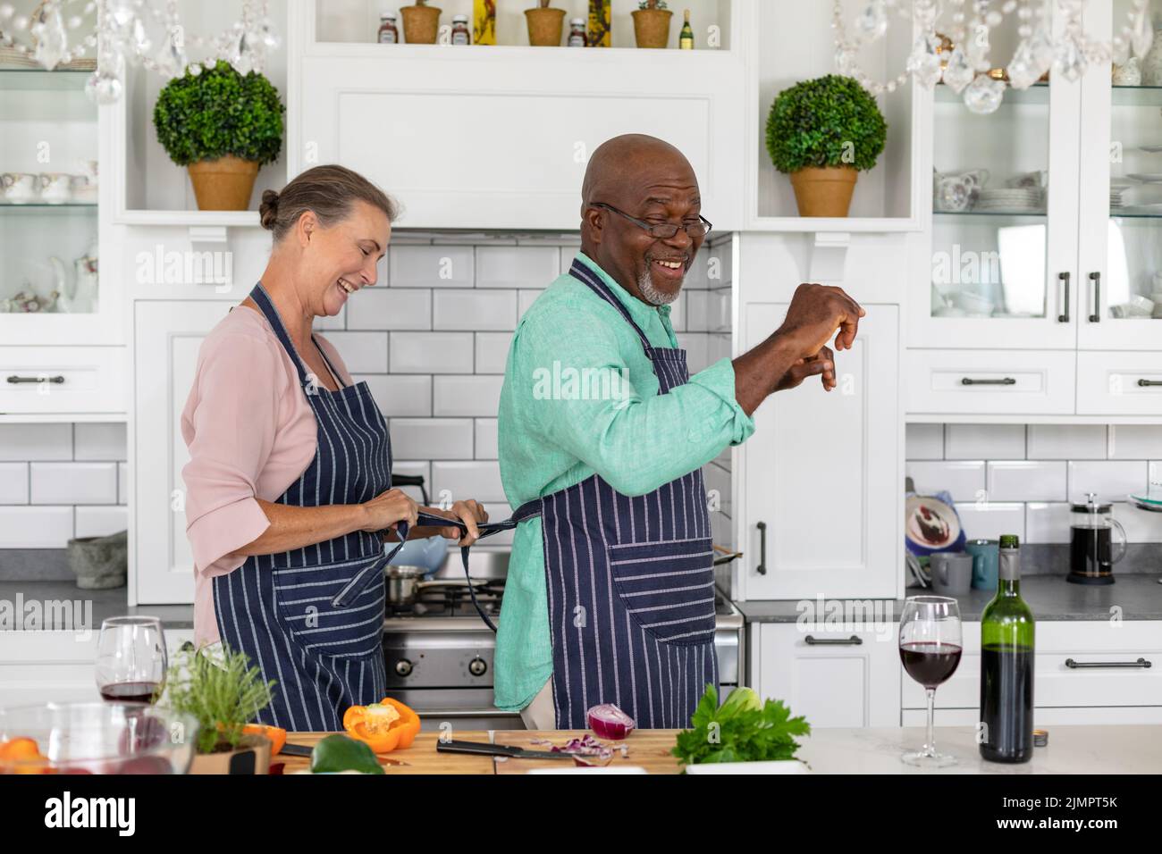 Happy multiracial senior couple dancing in kitchen while cooking food ...