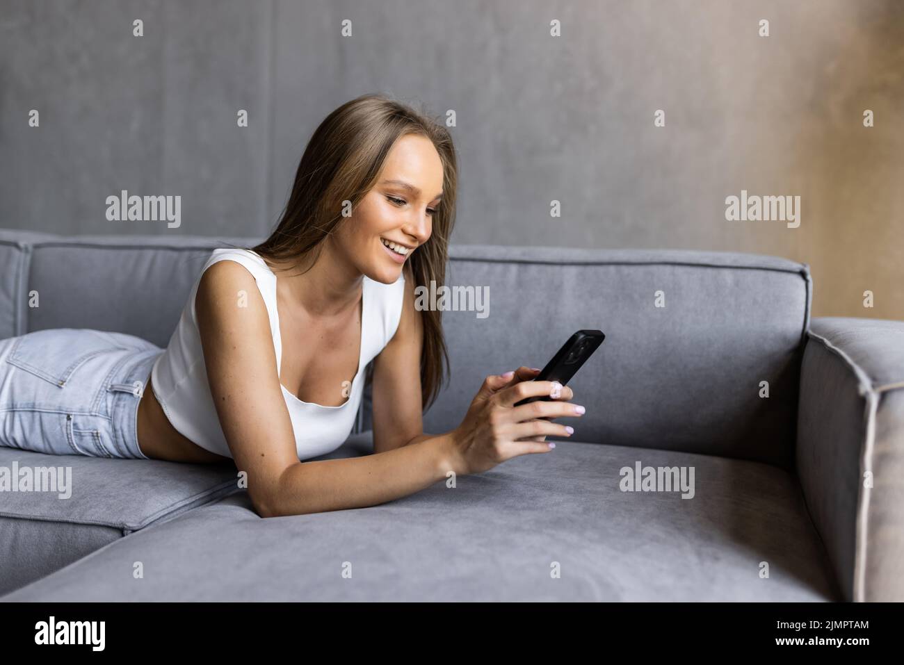Smiling young woman using mobile phone while sitting on a couch at home ...