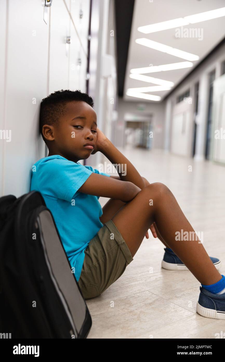 Portrait of sad african american elementary boy sitting on floor in ...