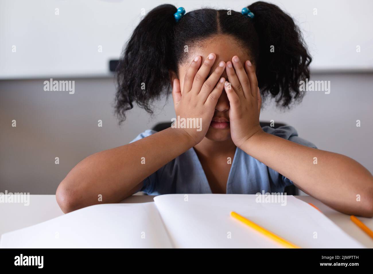 Depressed biracial elementary schoolgirl with hands covering face ...