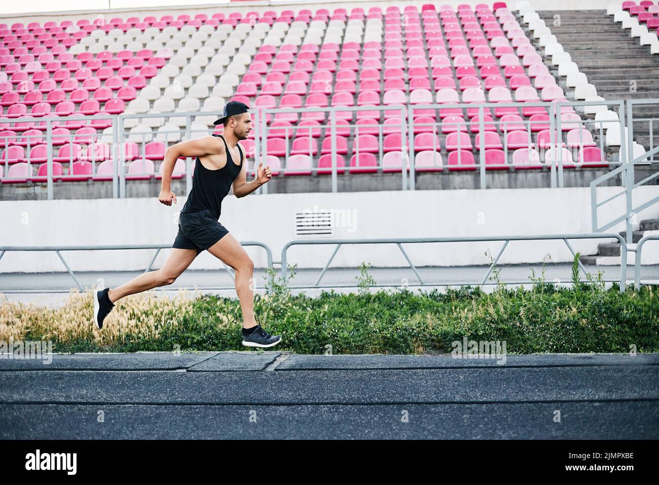 Athlete man running on the running track over empty seats in a sport ...