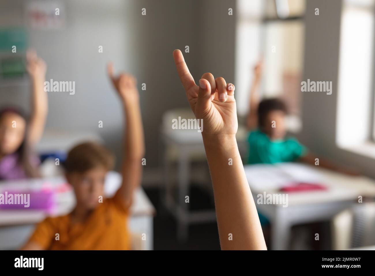 Multiracial elementary school students with hands raised during class ...