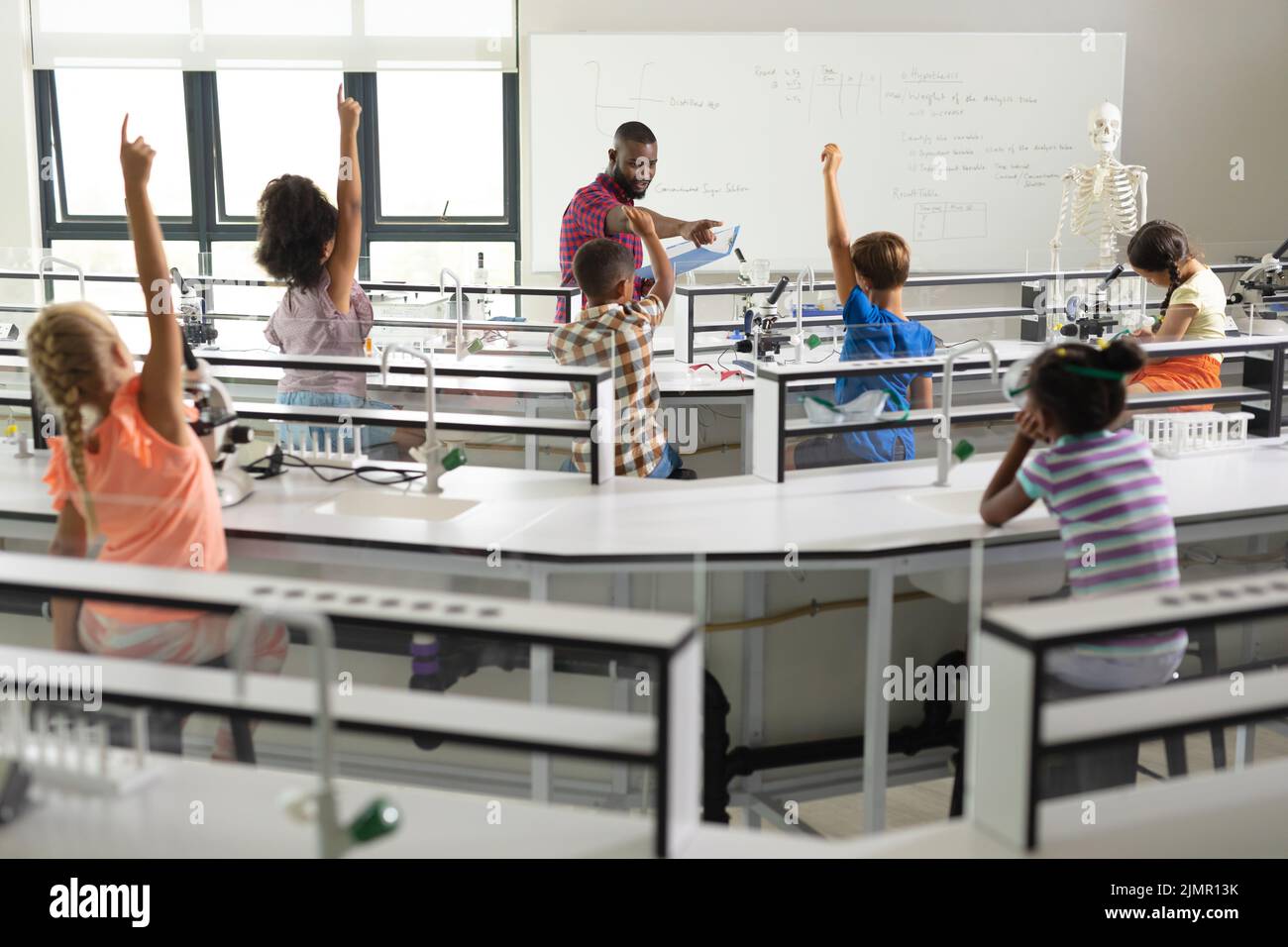 Multiracial elementary students raising hands while african american ...