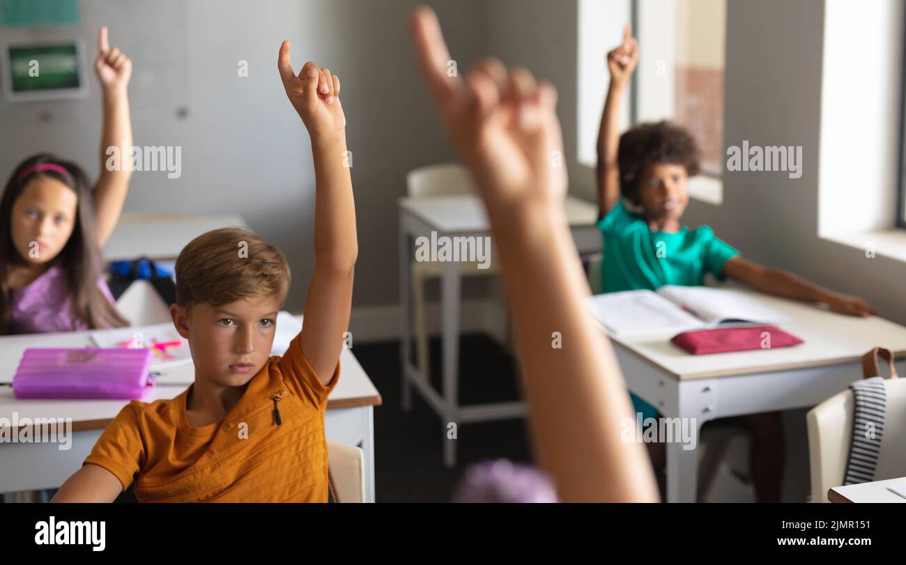 Multiracial elementary school students raising hands during class in ...