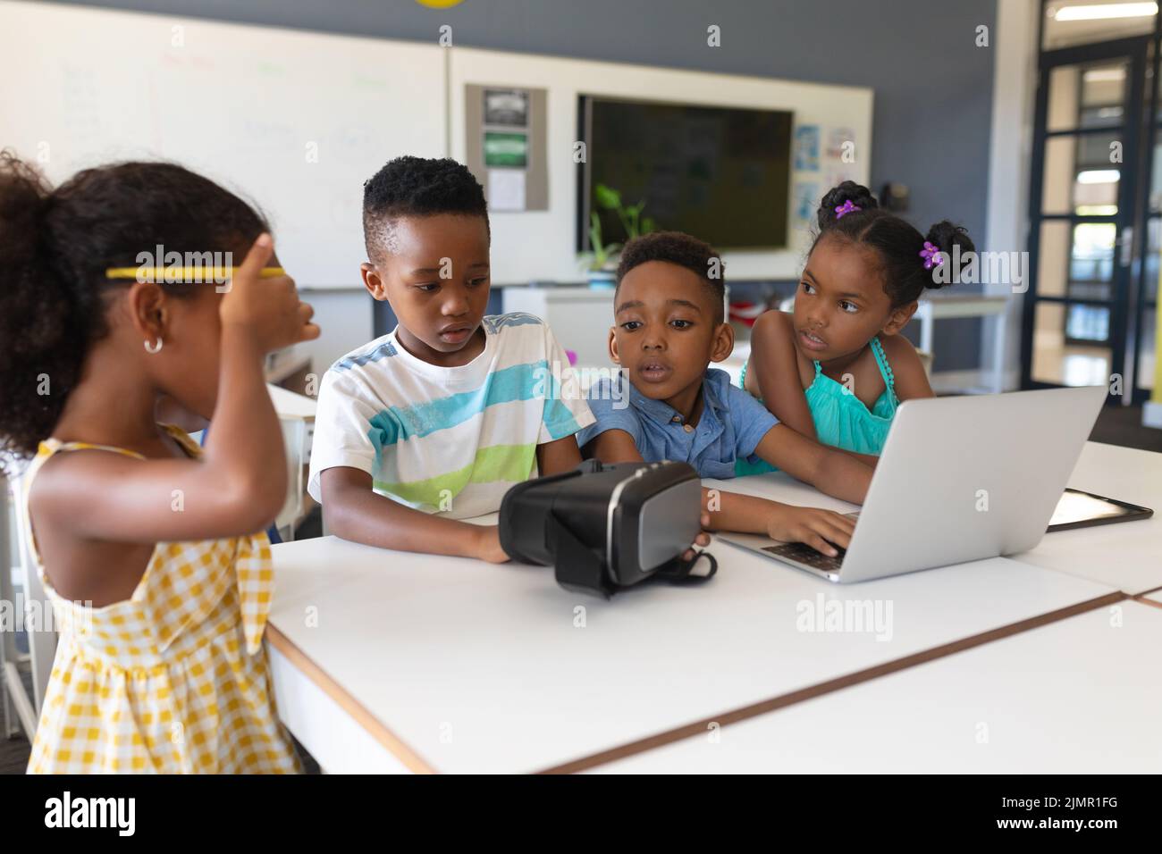 African american elementary school students using vr glasses and laptop ...