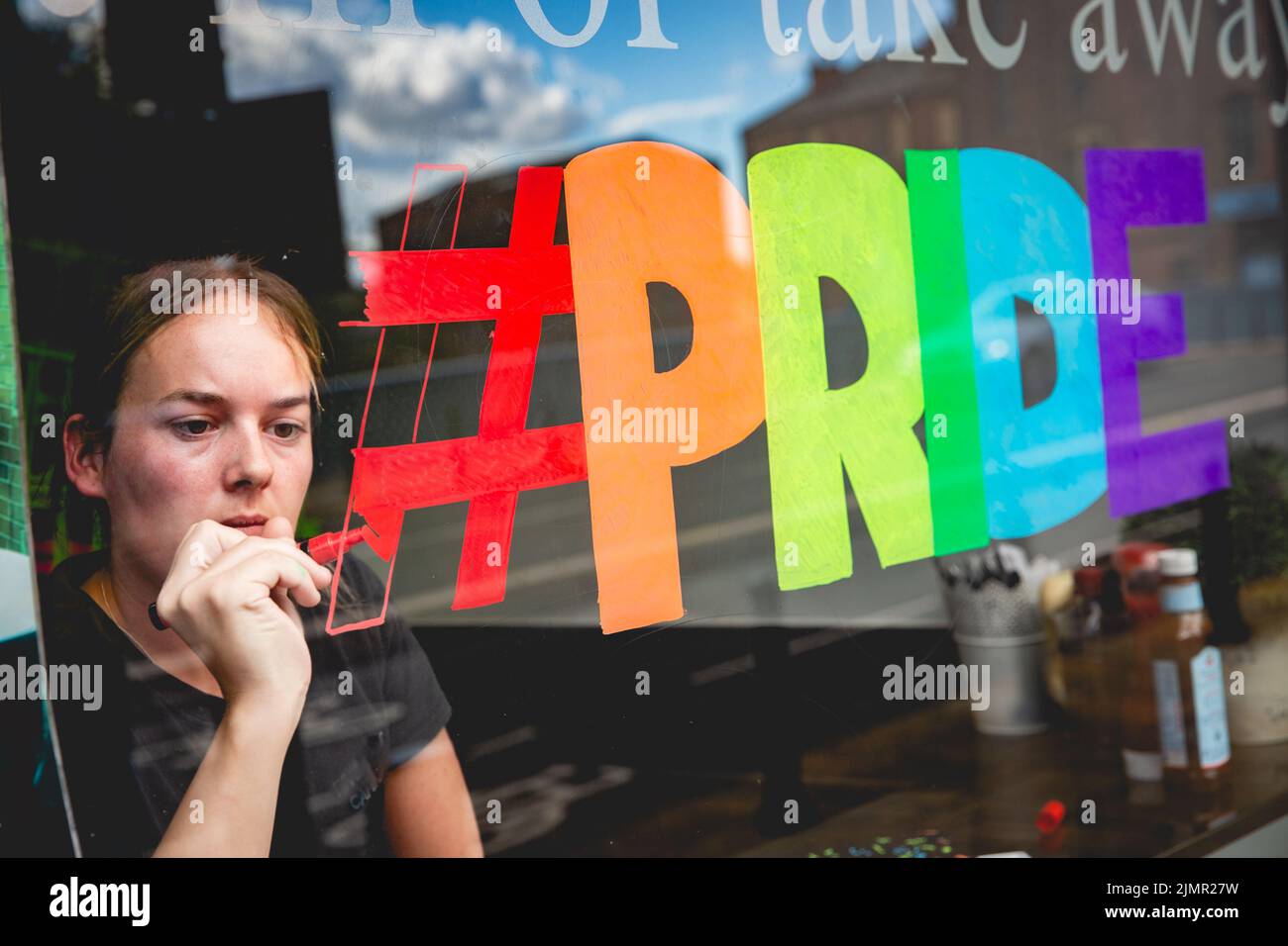 A girl decorating a store window with a colourful rainbow Gay Pride ...