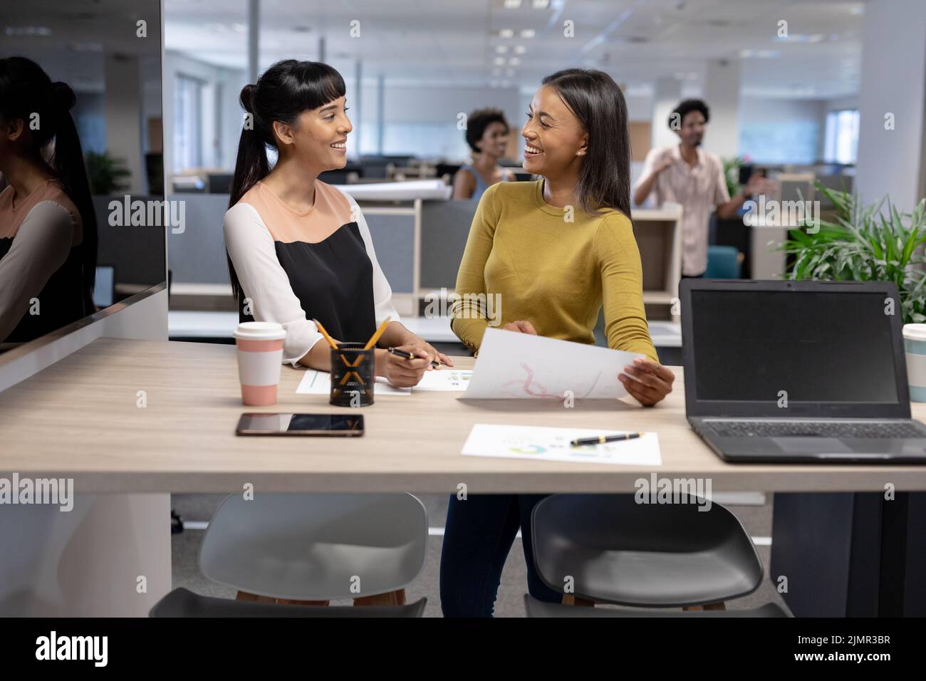 Happy multiracial businesswomen discussing over document while working ...