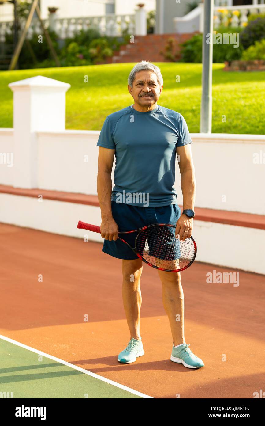 Portrait of confident biracial senior man holding tennis racket while ...
