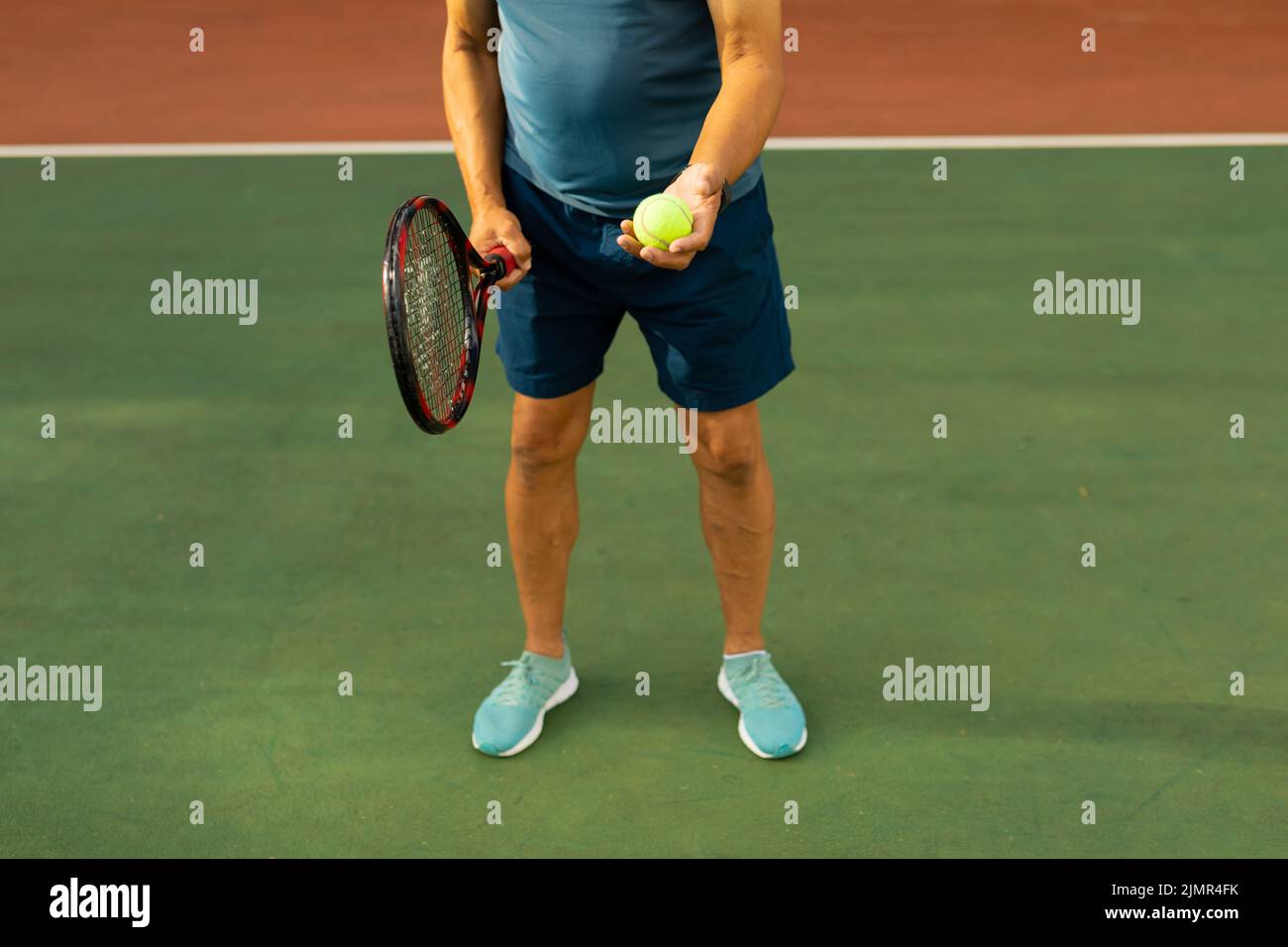 Low section of biracial senior man holding tennis racket and ball while ...