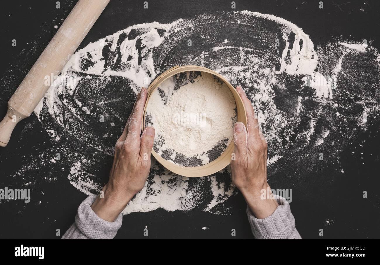Female hands hold a round wooden sieve with white wheat flour on a ...