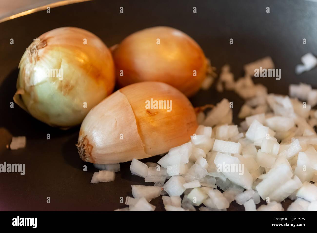 A closeup shot of unpeeled onions and cut onions in a frying pan ...