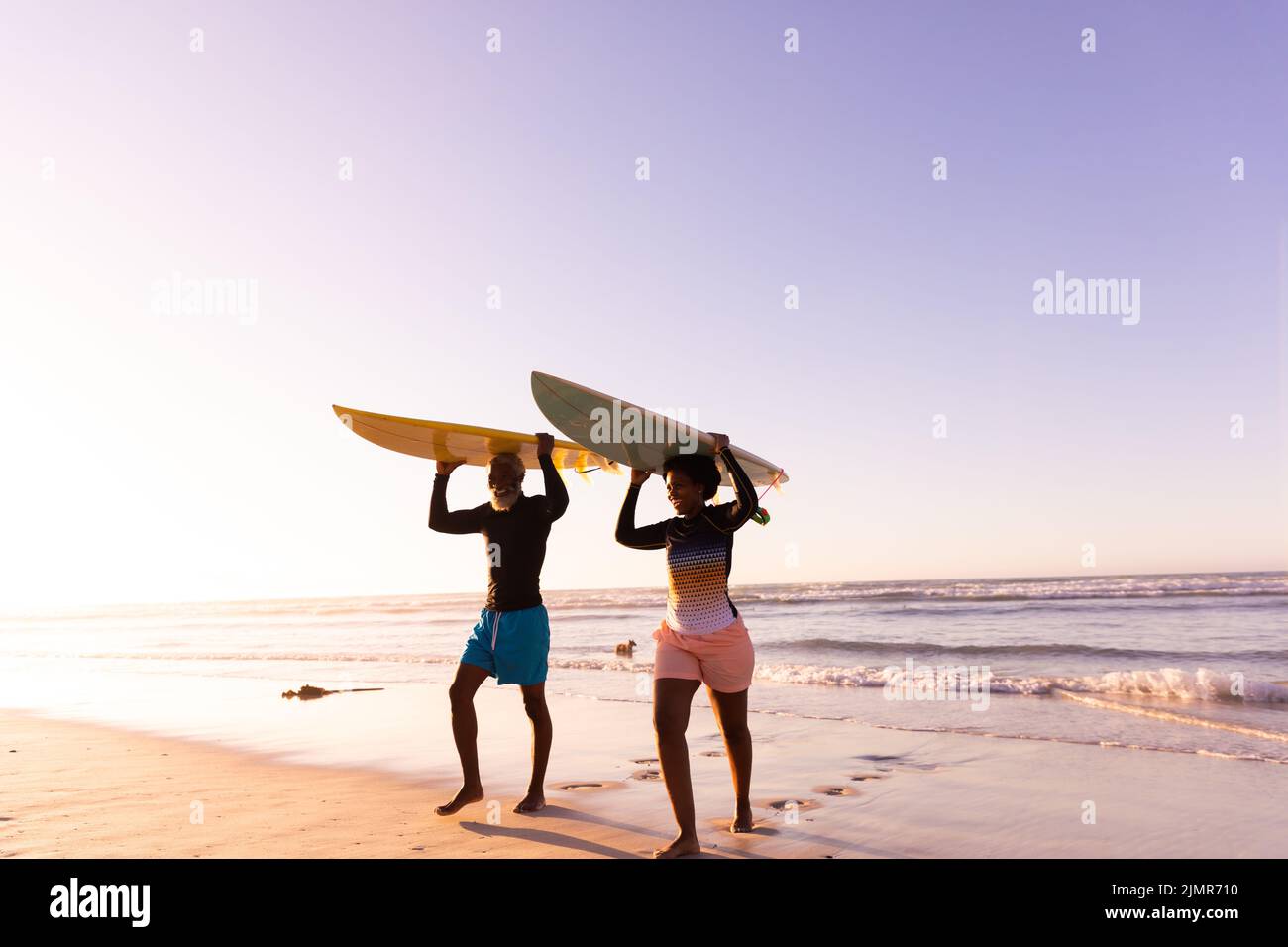 African american couple carrying surfboards on heads while walking ...