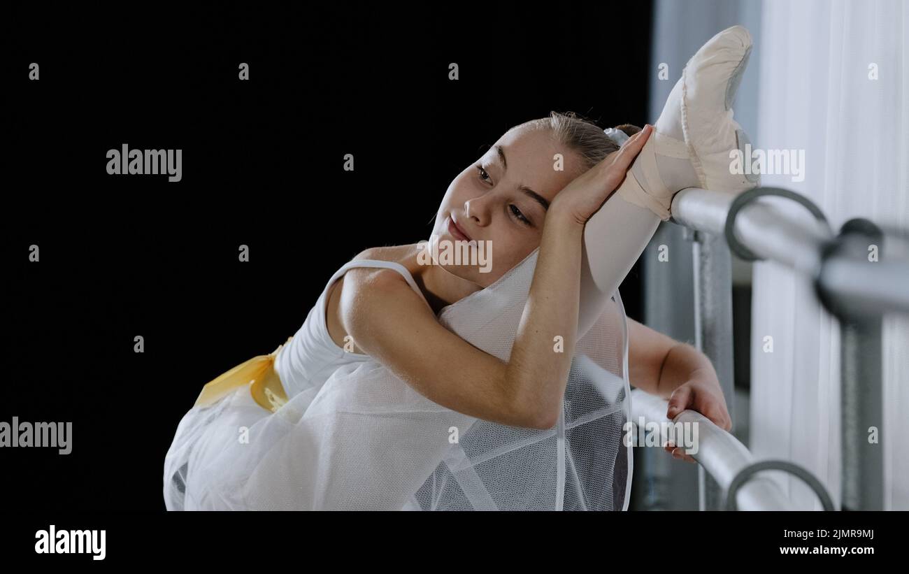 Flexible ballerina girl child in ballet tutu stretches near barre in ...