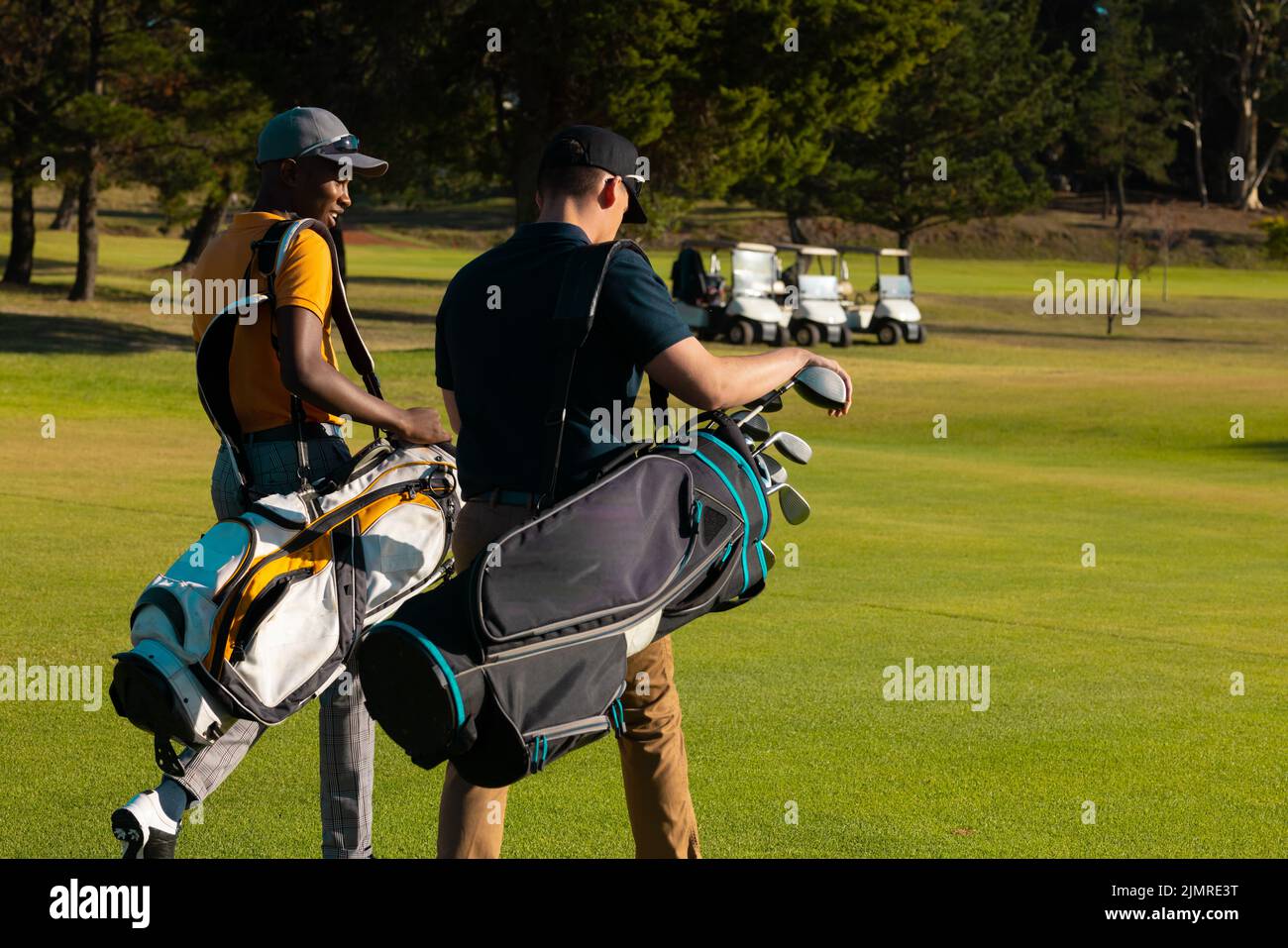 Young male multiracial friends wearing caps with golf bags walking at ...