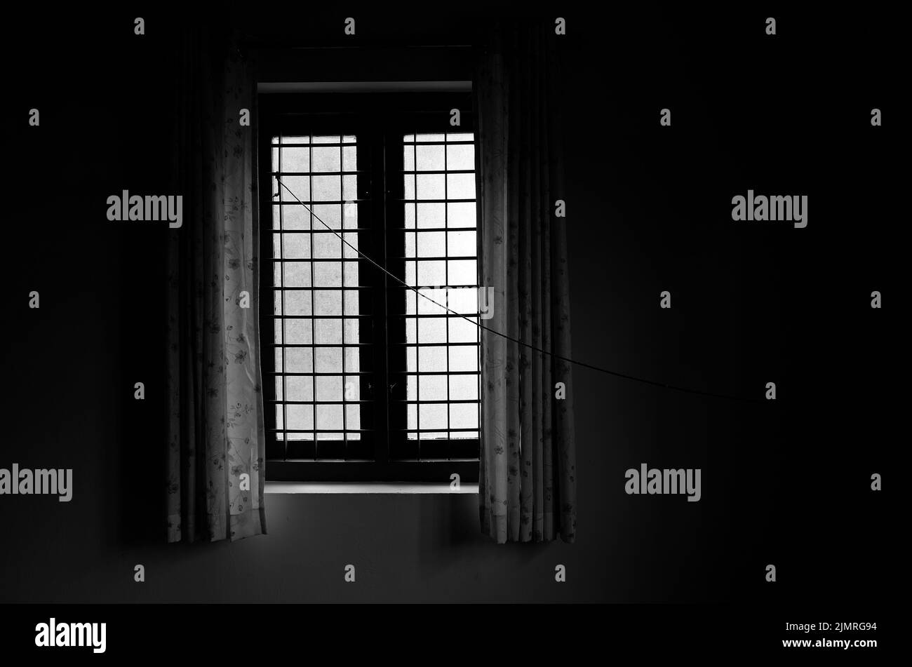 A Grayscale Of A Window With Metal Lattice Bars And Curtains Stock
