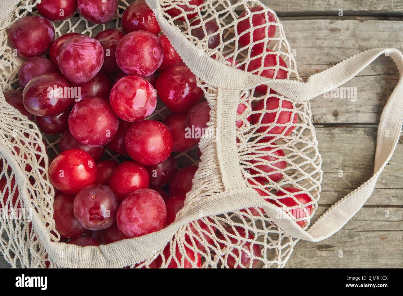 Juicy plums in eco friendly string eco mesh bag on a wooden background ...