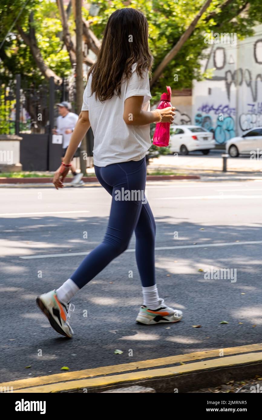 A vertical shot of a young woman jogging on a street on a sunny day ...