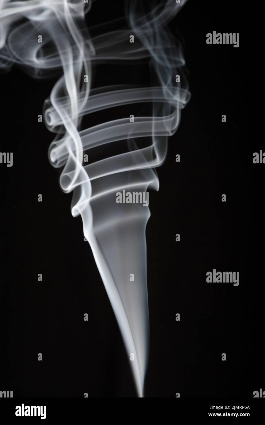 Puffs and curls of white smoke against a black background rising from a ...