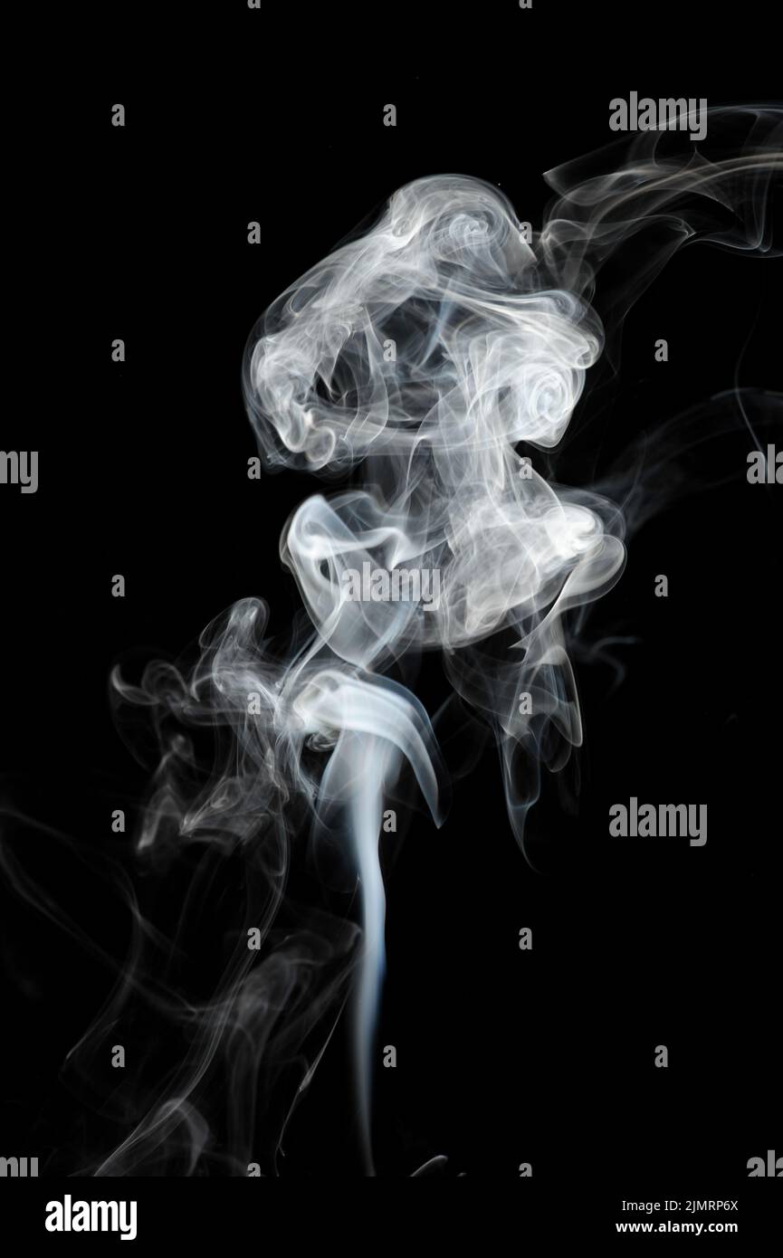 Puffs and curls of white smoke against a black background rising from a ...