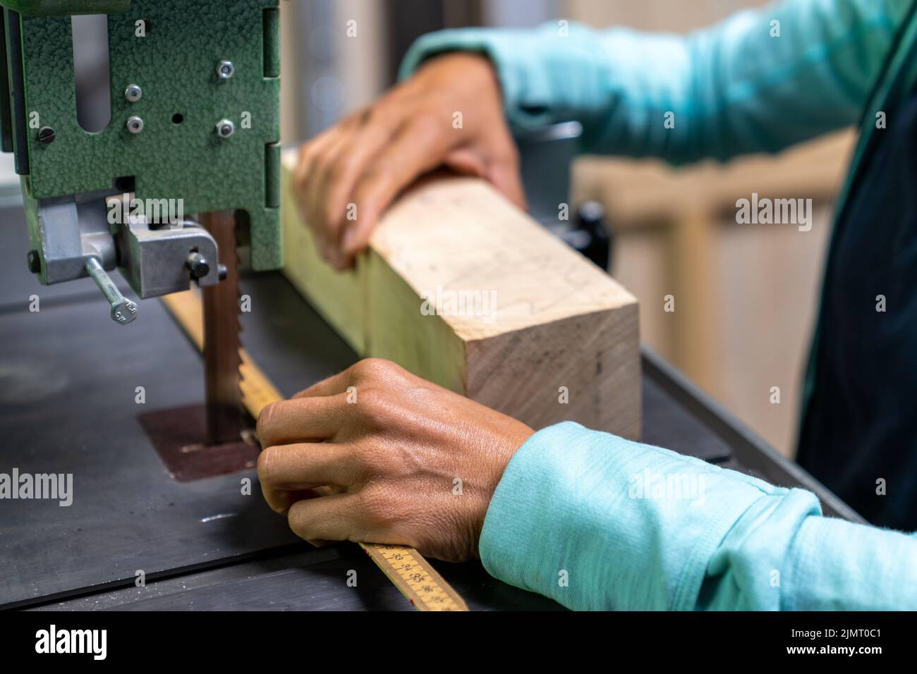 A close-up of a woman carpenter cutting a block of wood with a band saw ...