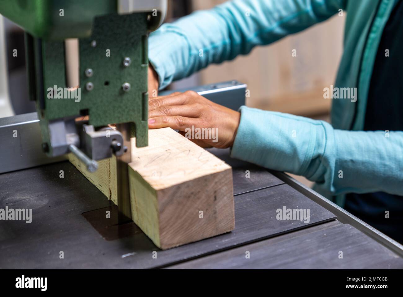 A close-up of a woman carpenter cutting a block of wood with a band saw ...