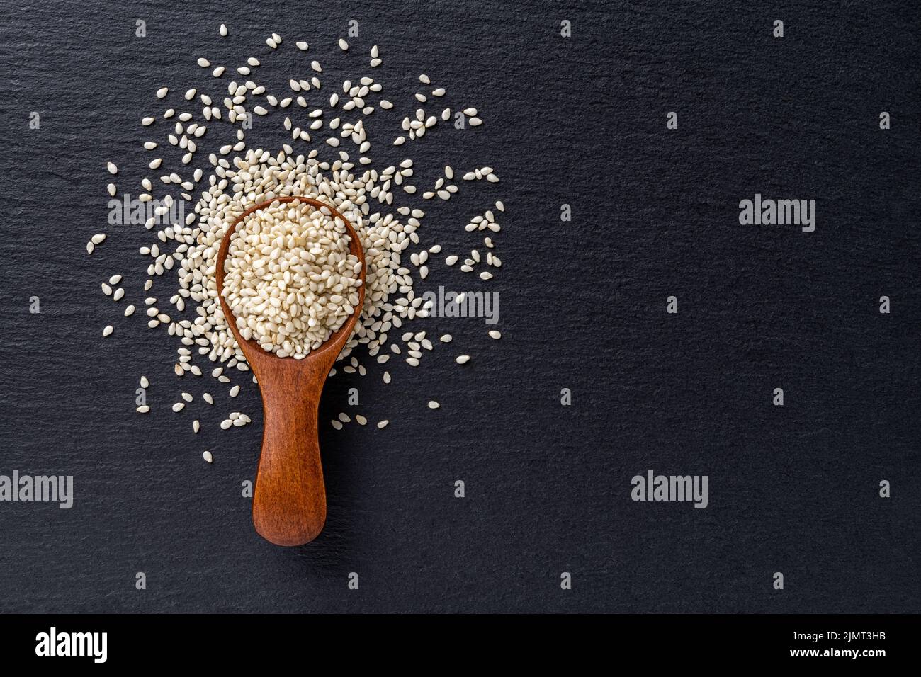 Raw sesame seeds in a wooden spoon over black slate background. Sesamum ...