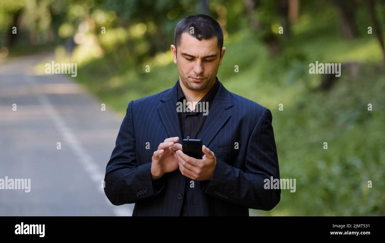 Serious adult caucasian man user stand outdoors in park wears black ...