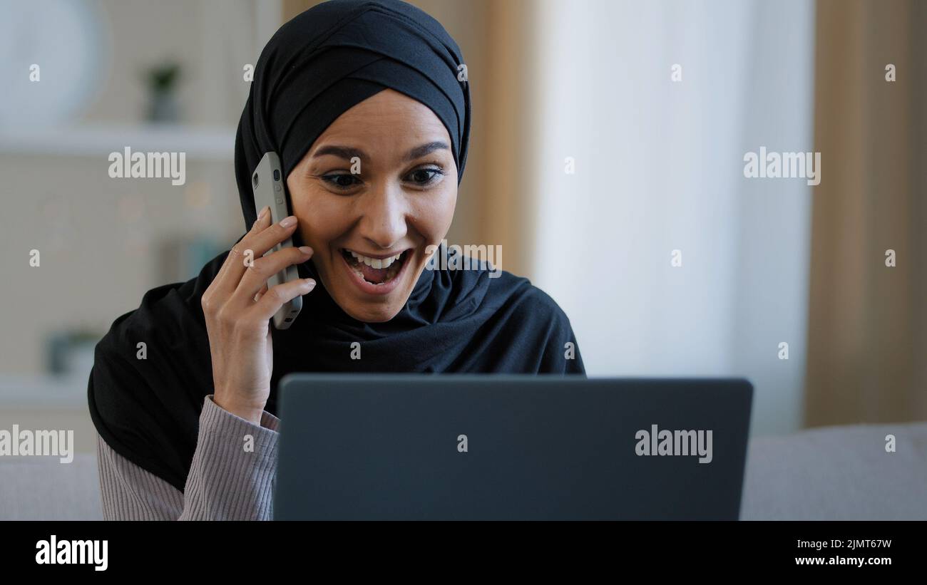 Happy smiling arabian woman muslim girl in hijab female freelancer talking by mobile phone with ...