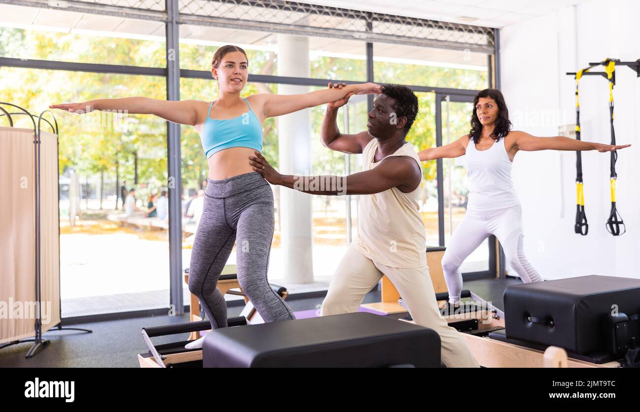 Woman coach helping man and woman in pilates workout Stock Photo - Alamy