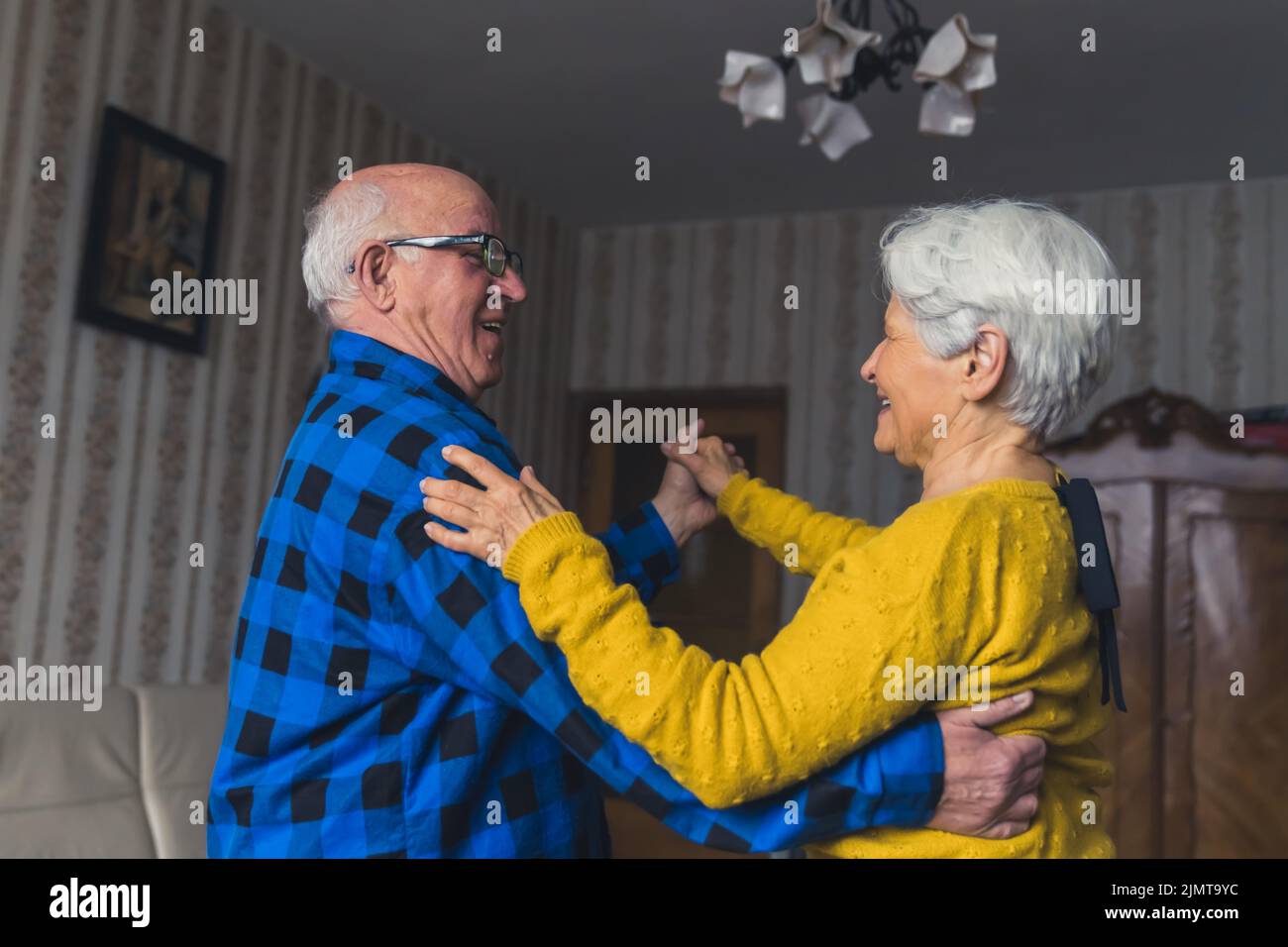 Happy romantic old married couple laughing and dancing in the living room, holding hands, having ...