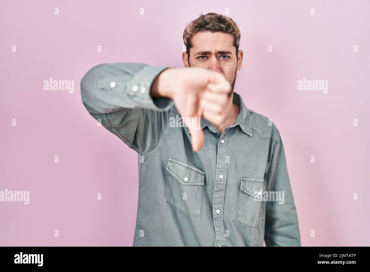 Hispanic man with beard standing over pink background looking unhappy ...