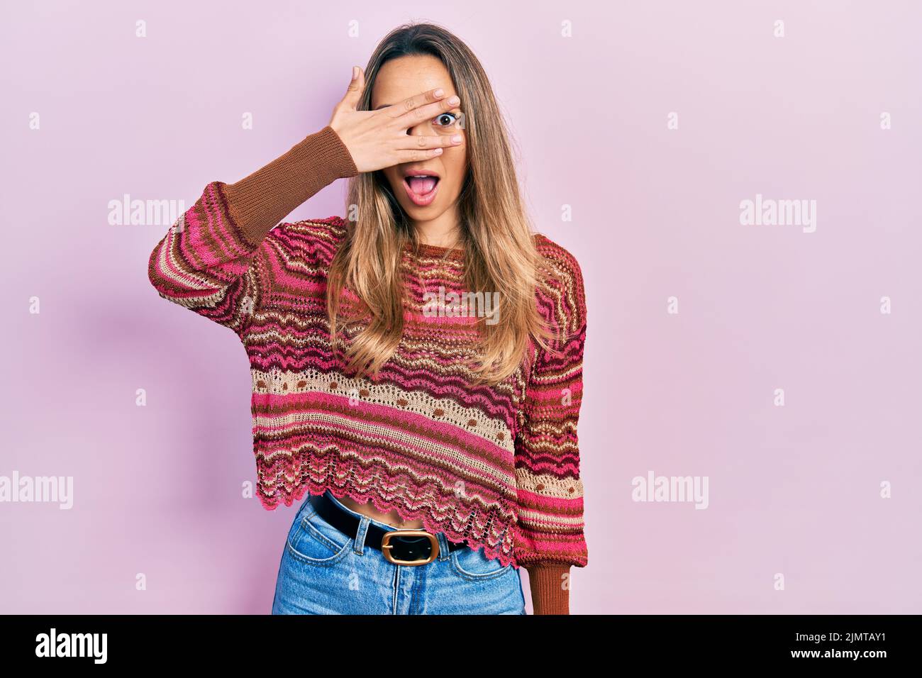 Beautiful hispanic woman wearing hippie sweater peeking in shock ...