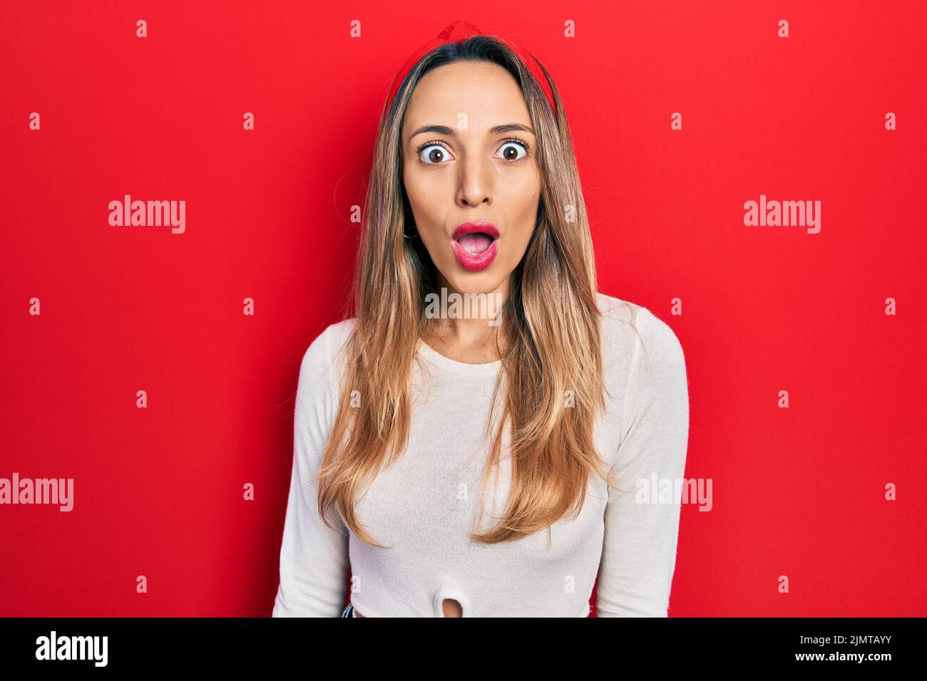 Beautiful hispanic woman wearing red diadem afraid and shocked with ...