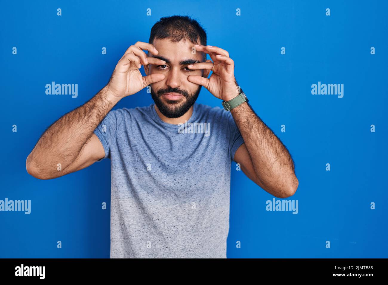 Middle east man with beard standing over blue background trying to open ...