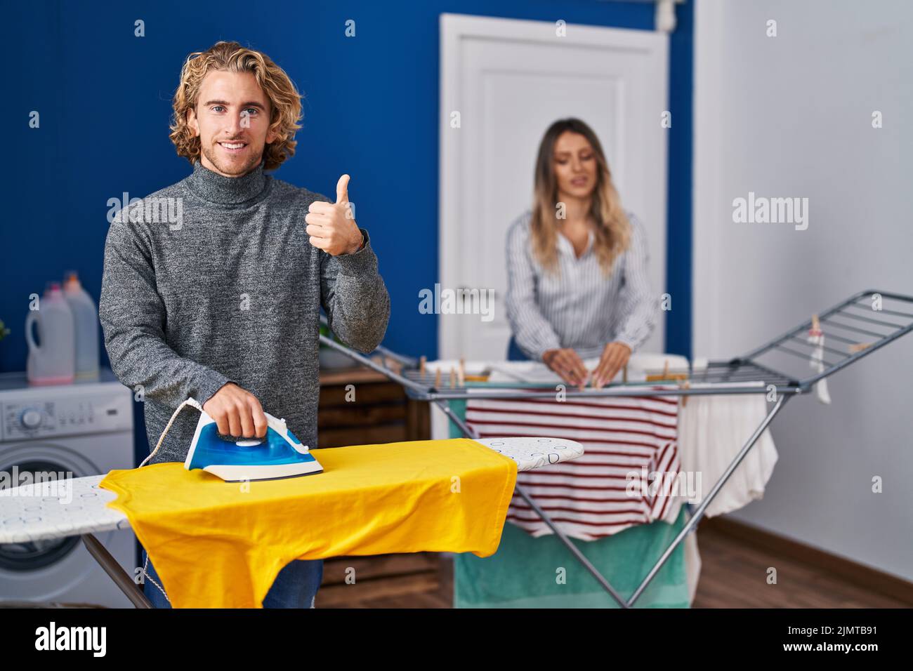 Couple ironing clothes at laundry room smiling happy and positive ...