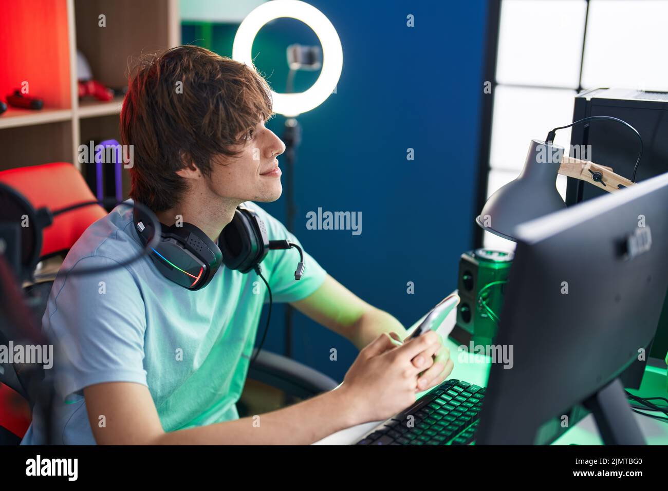 Young blond man streamer using computer and smartphone at gaming room ...