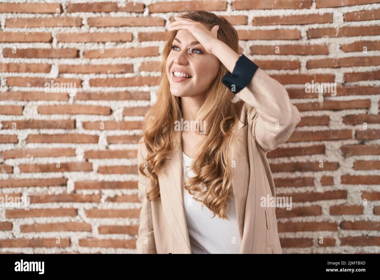 Beautiful blonde woman standing over bricks wall very happy and smiling ...